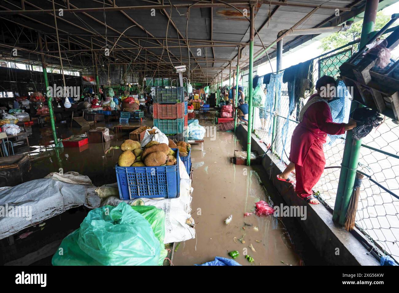 A Nepalese woman walks along edges of a flooded vegetable market as a ...