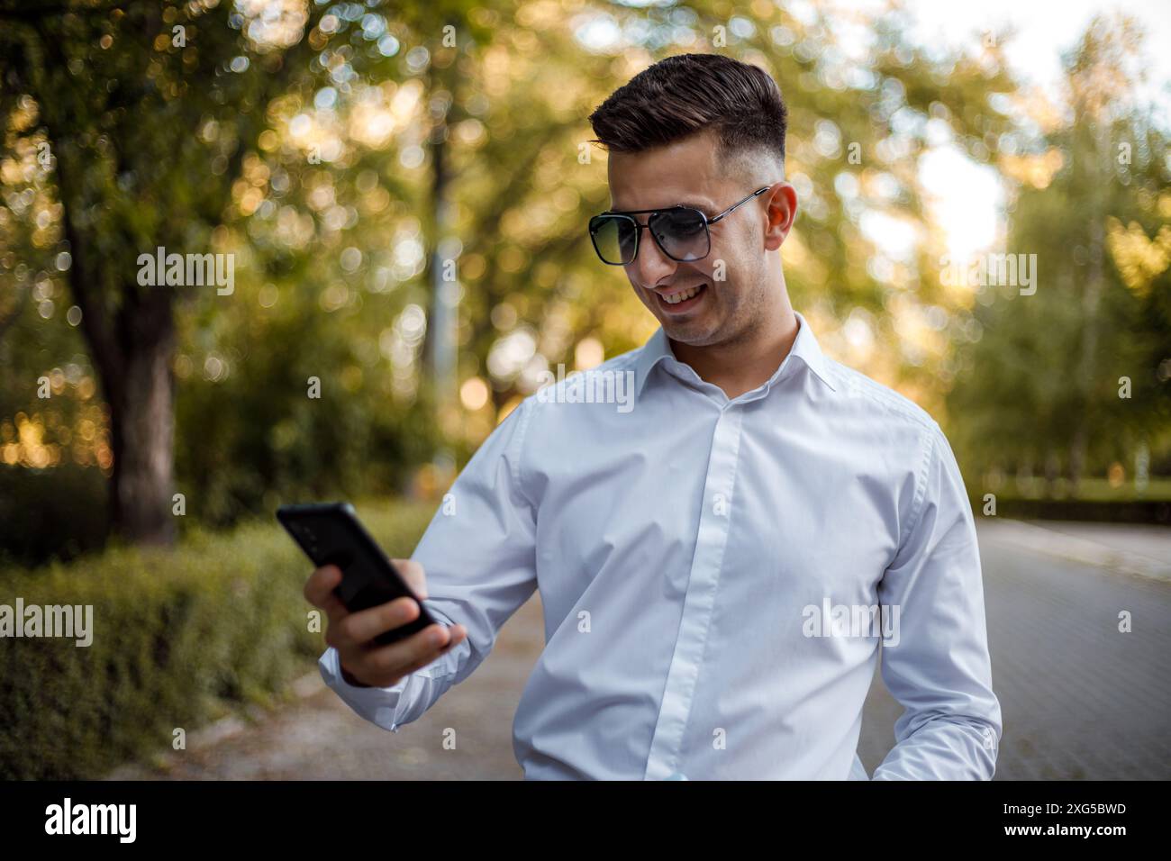 A man wearing sunglasses is focused on his cell phone screen, scrolling and reading intently ...