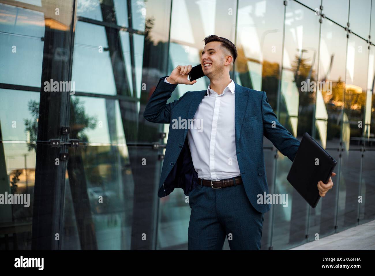 A man wearing a suit and white shirt stands in front of a modern glass ...