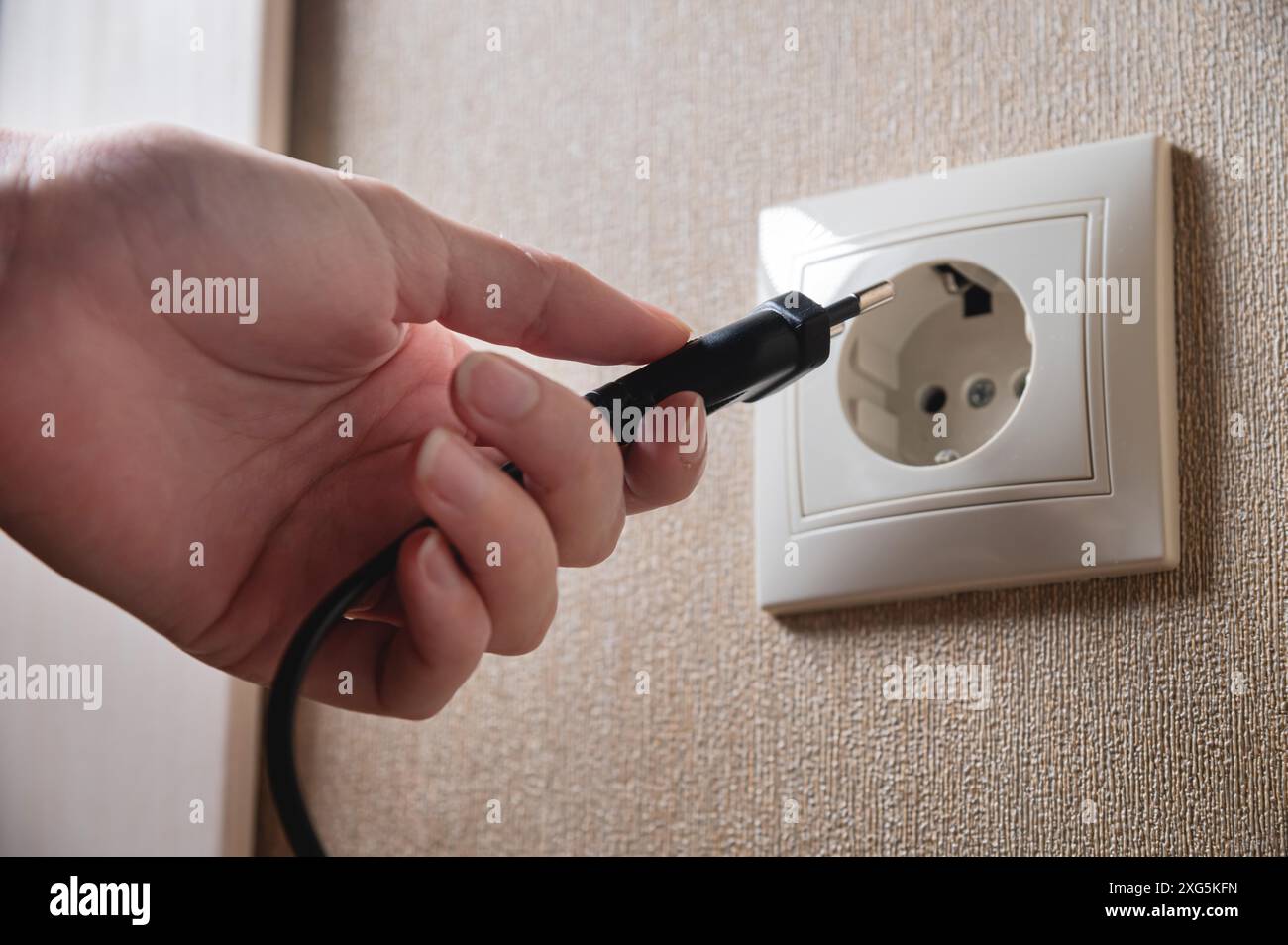 A female hand inserts an electric plug into a euro-format socket close ...
