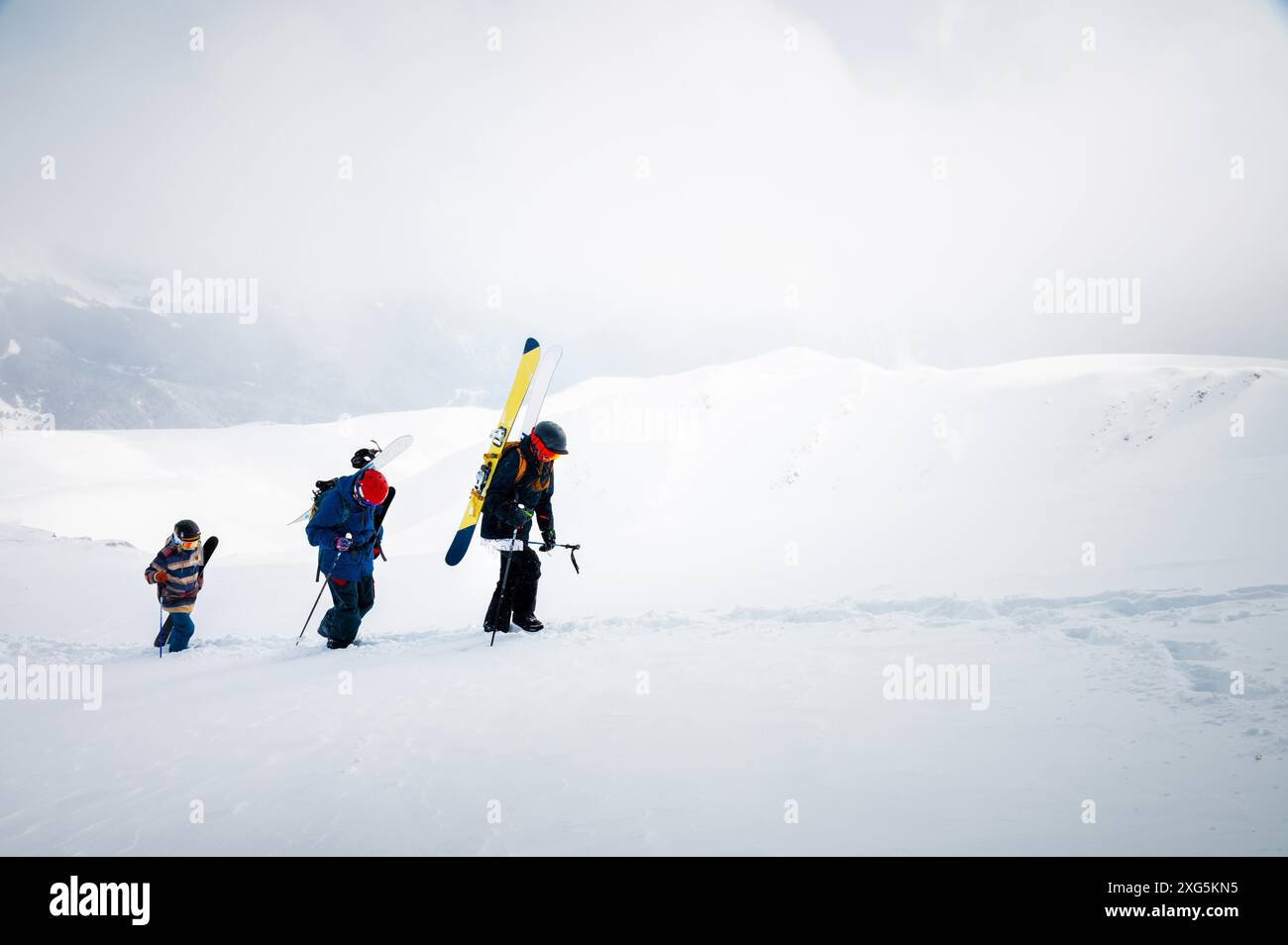 Three friends snowboarders skiers go uphill with a snowboard and skis ...