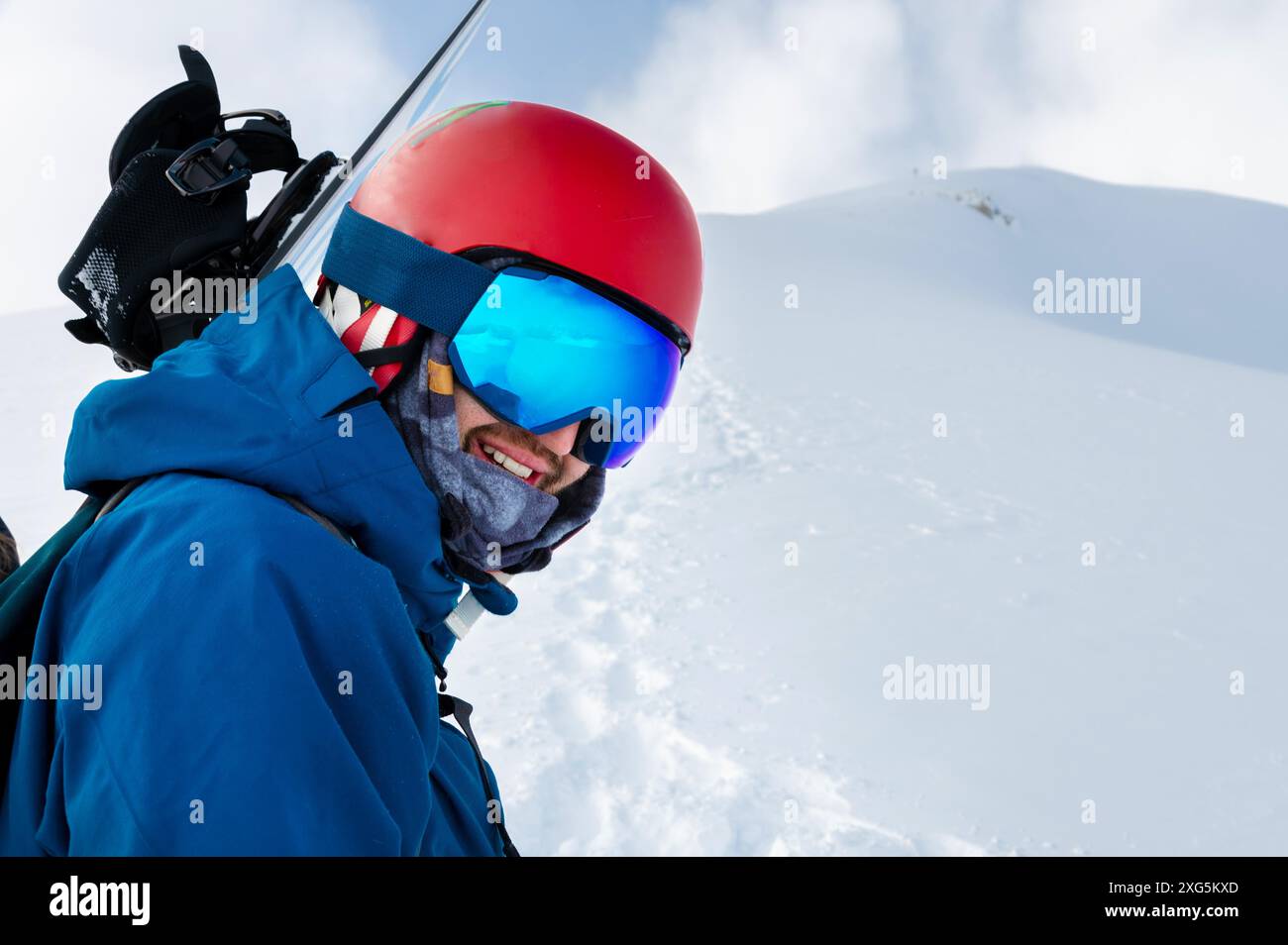 Equipped skier holding skis on his shoulder and looking directly at the ...