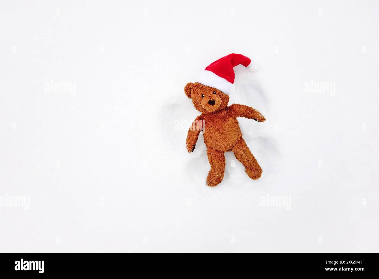 Snow angel, overhead view, cute teddy bear in red Santa hat having fun ...