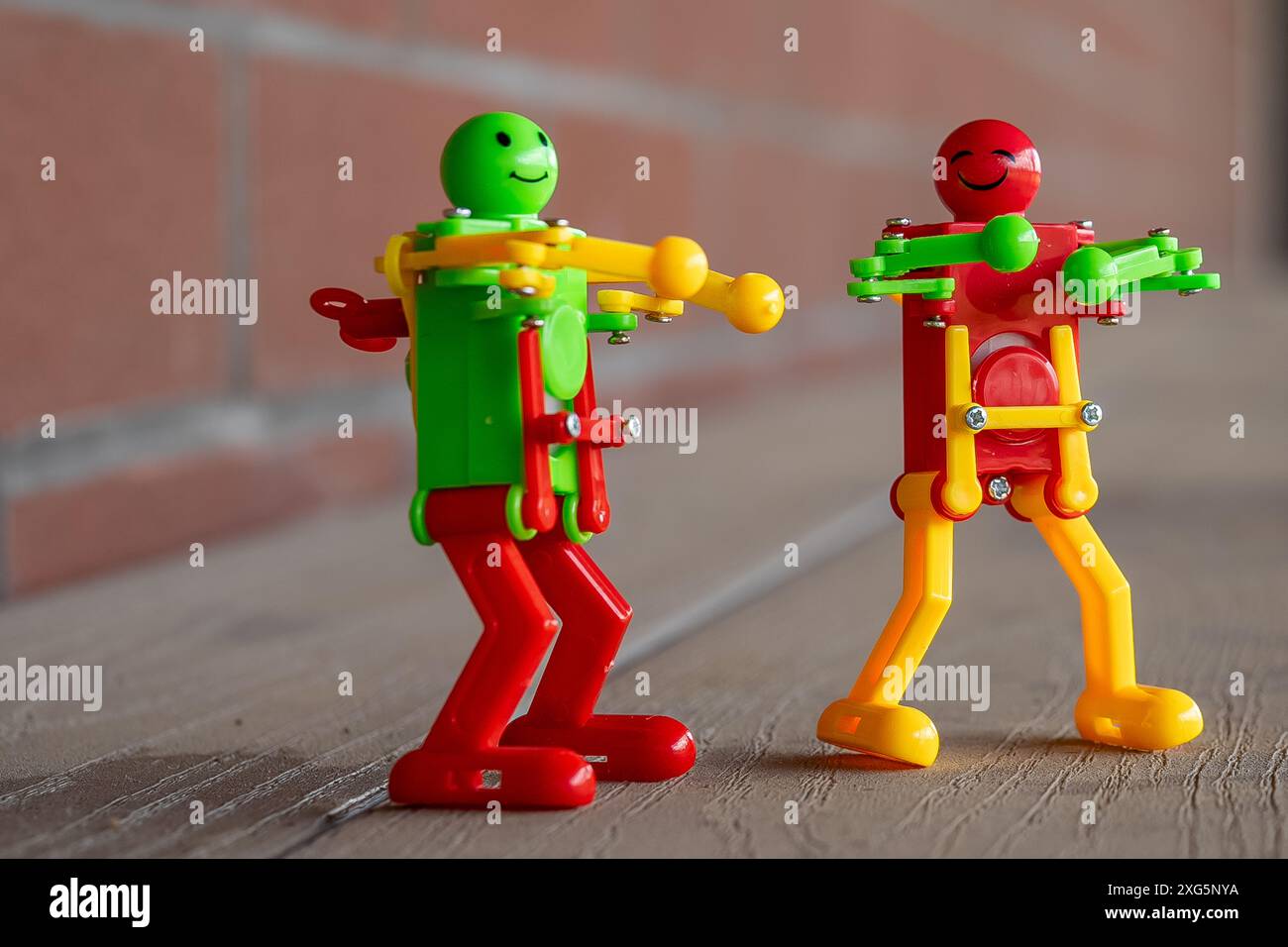 Two toy robots doing a happy dance, celebrating, on a wood surface ...
