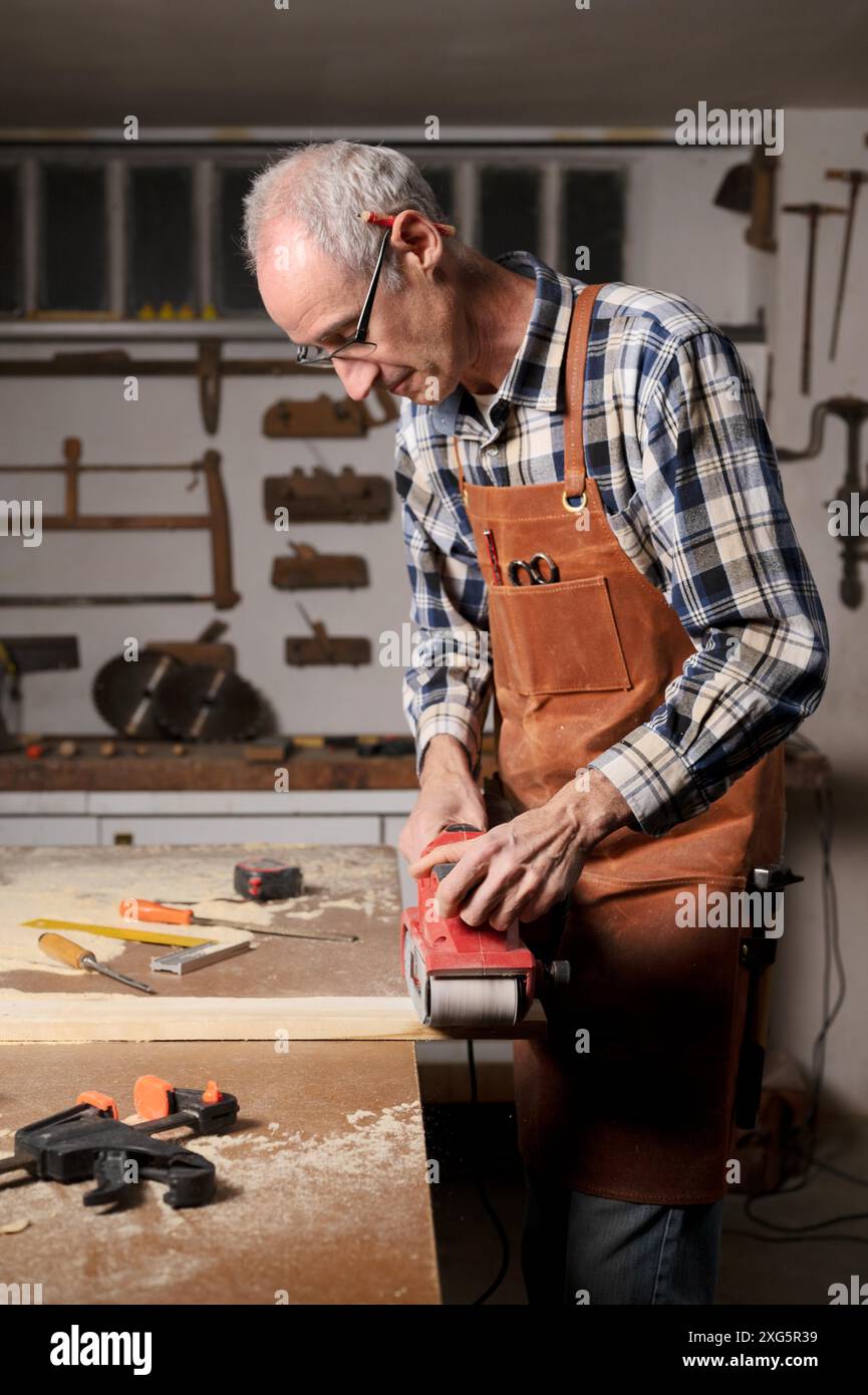 Carpenter sanding wood with belt sander at workshop in wooden board ...