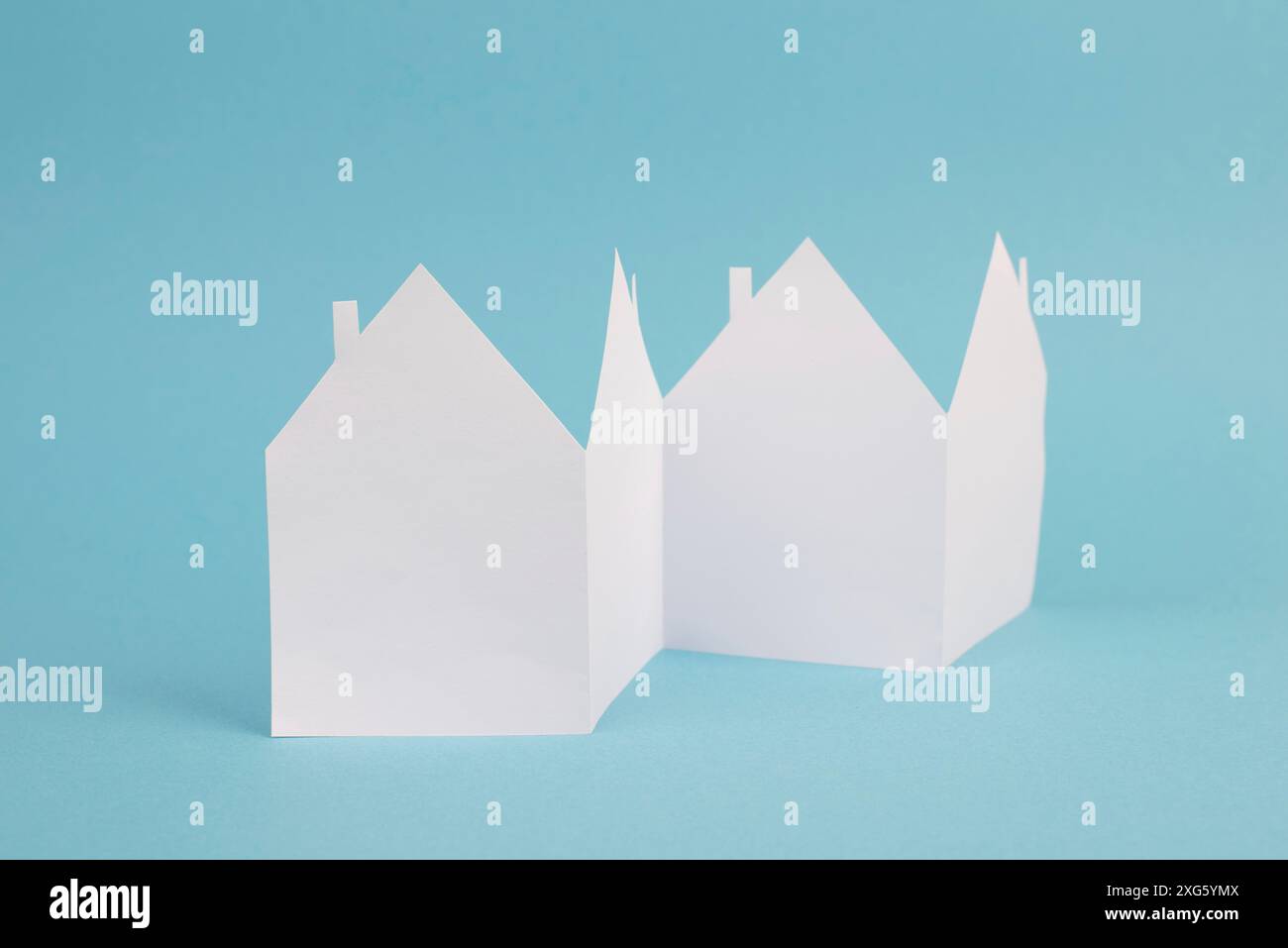 Row of white paper houses on a blue colored background, empty copy ...