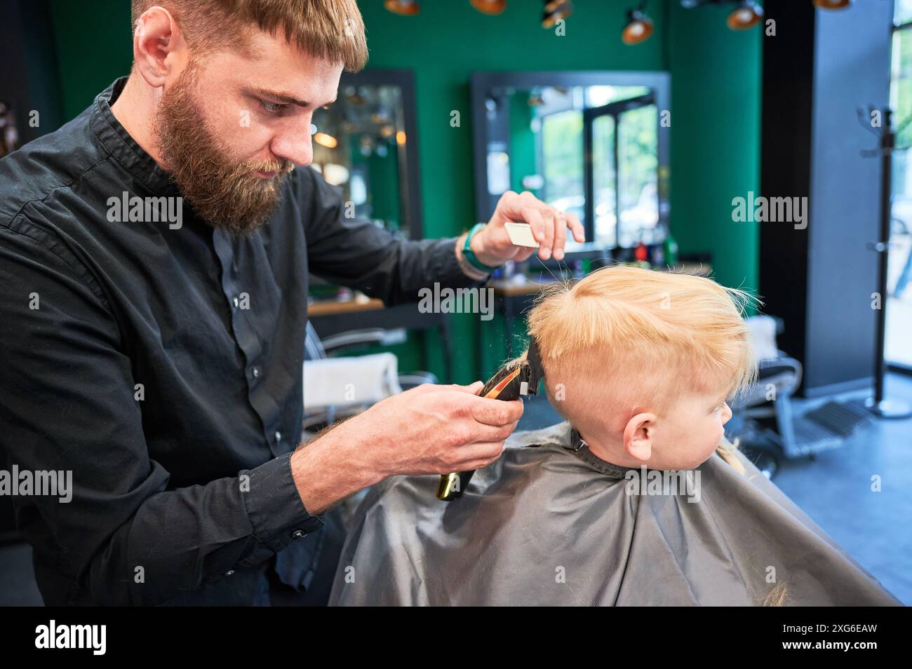 Professional hairdresser shaving boy's head, using shaver and comb ...