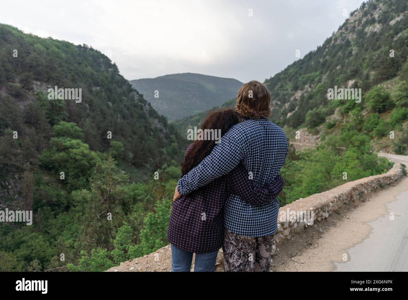 A couple is hugging each other while looking out over a mountain range ...