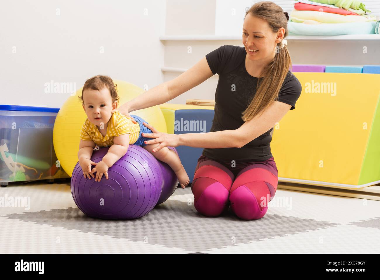 Happy child sitting on a violet fitness ball with his physiotherapist ...