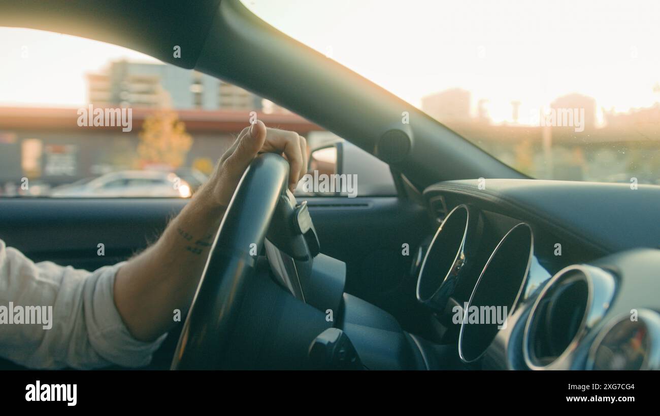 Close up male hands turning steering wheel driving vehicle in sunset ...