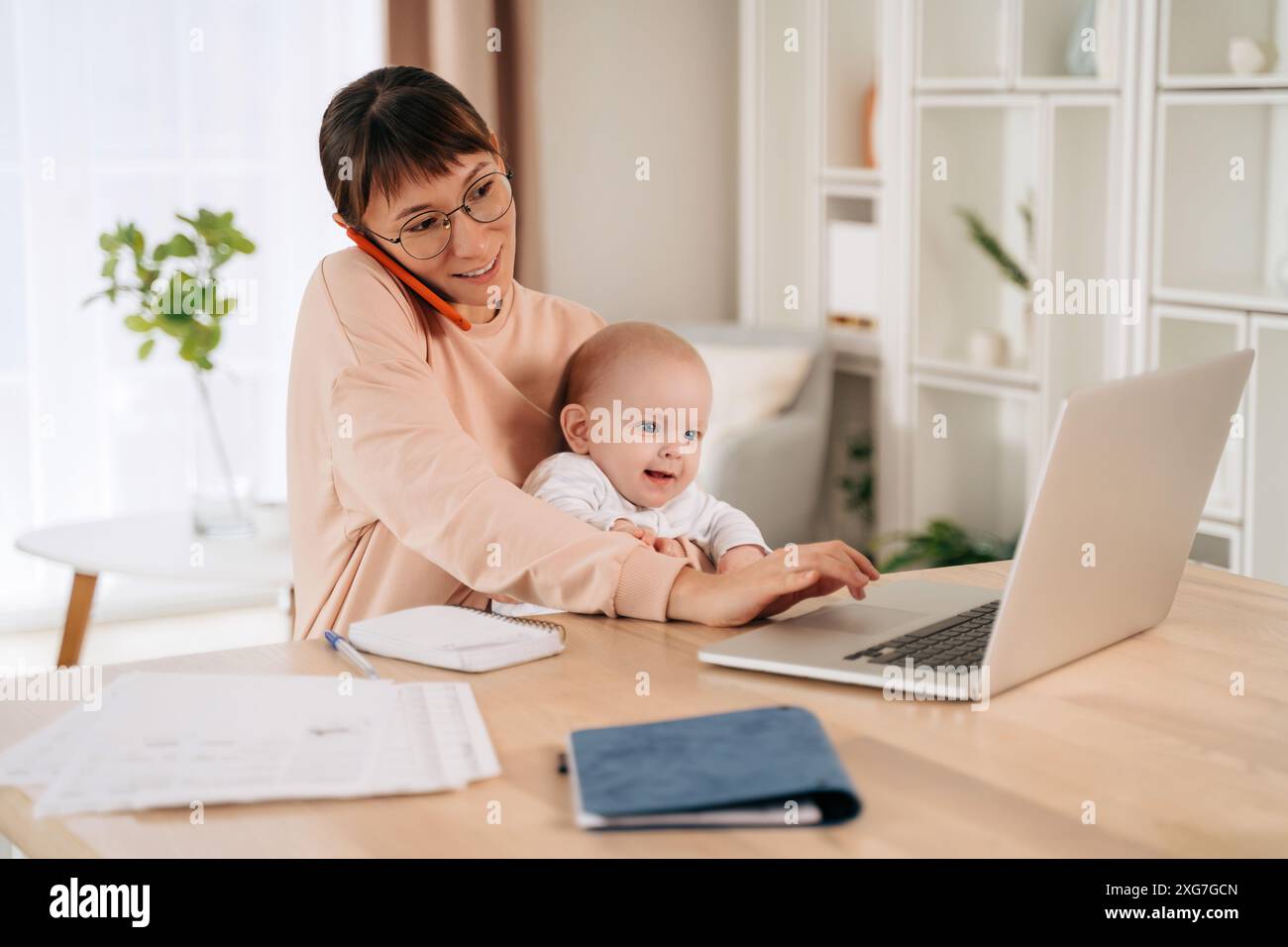 Single mother taking a phone call while holding her baby and using ...