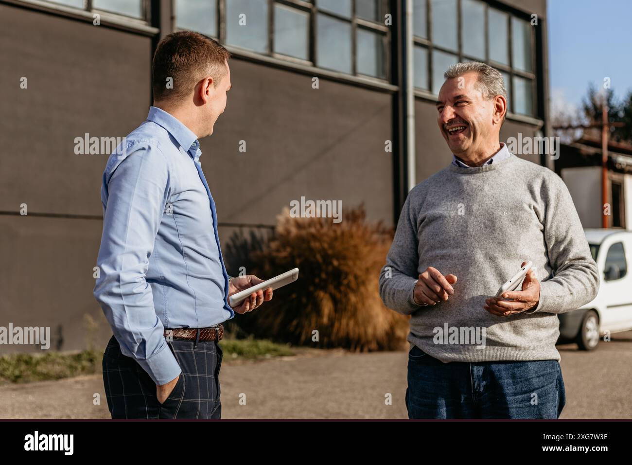 Two men are standing outside of an industrial building, engaged in ...