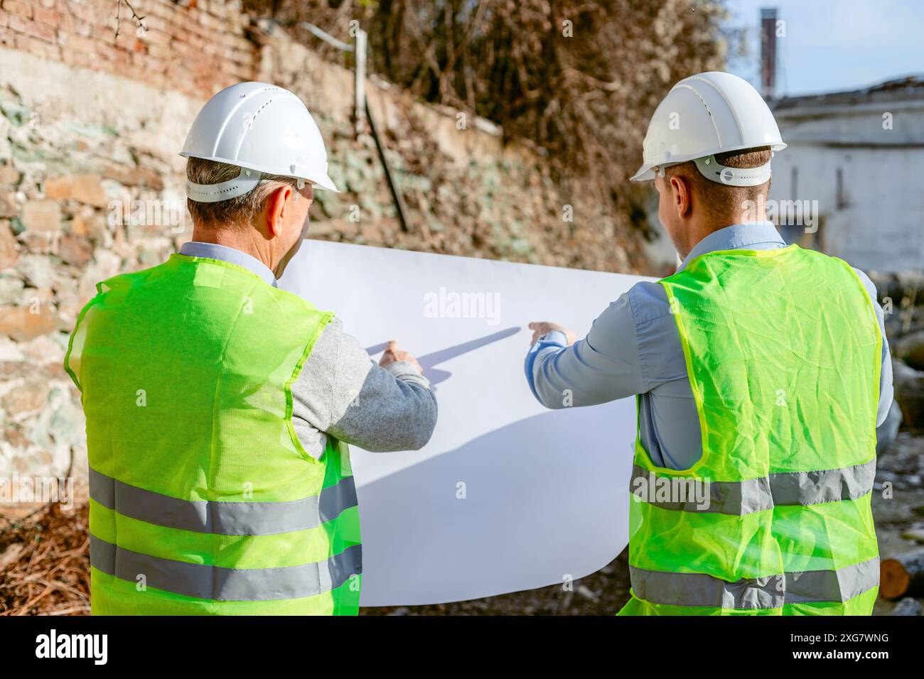 Two construction workers, wearing hard hats and safety vests, stand on ...