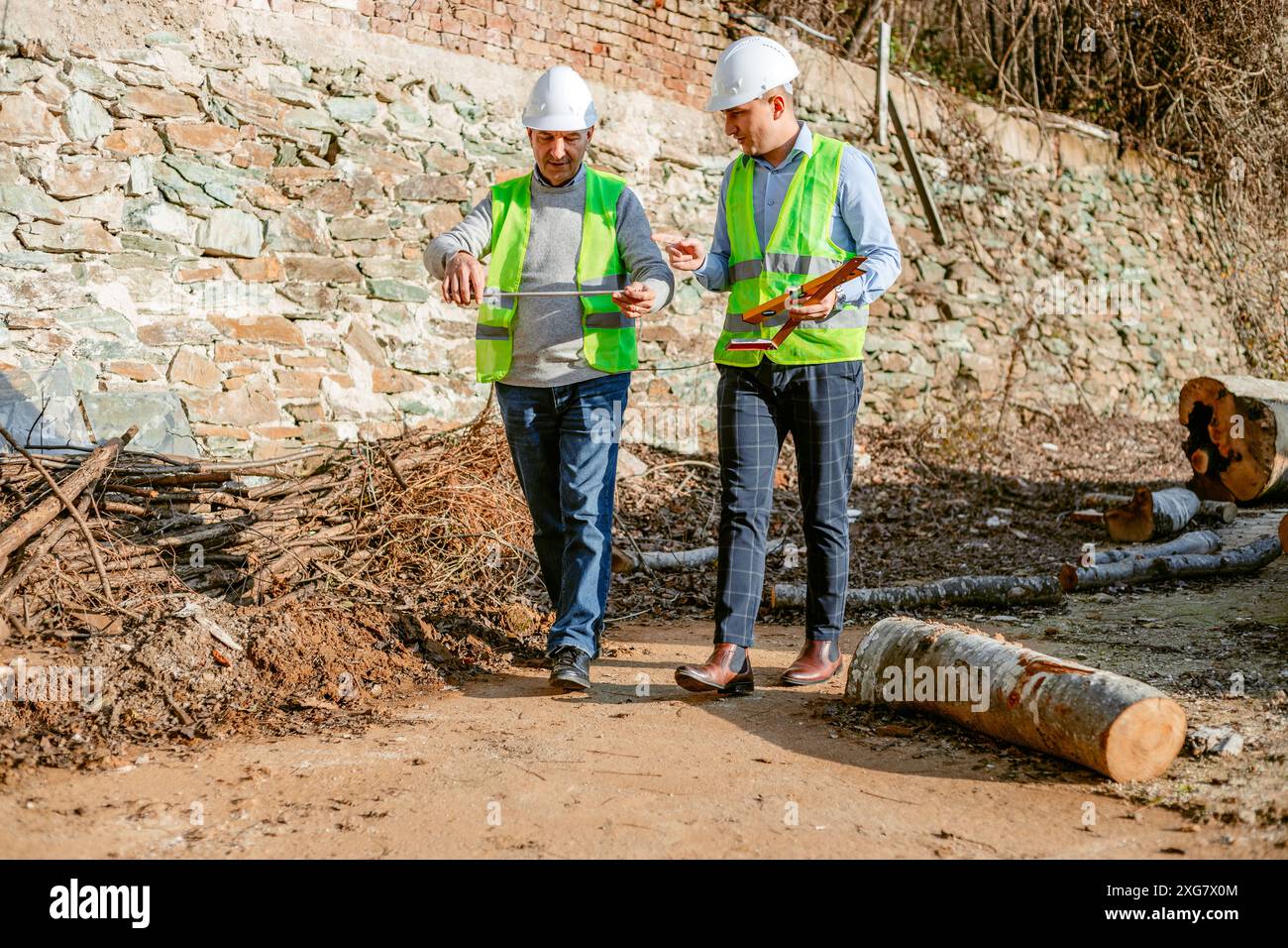 Two construction workers are walking on a dirt road at a construction ...