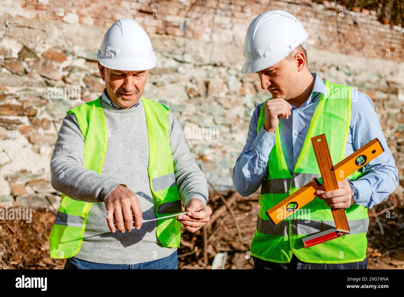 Two construction workers stand on a construction site, wearing hard ...