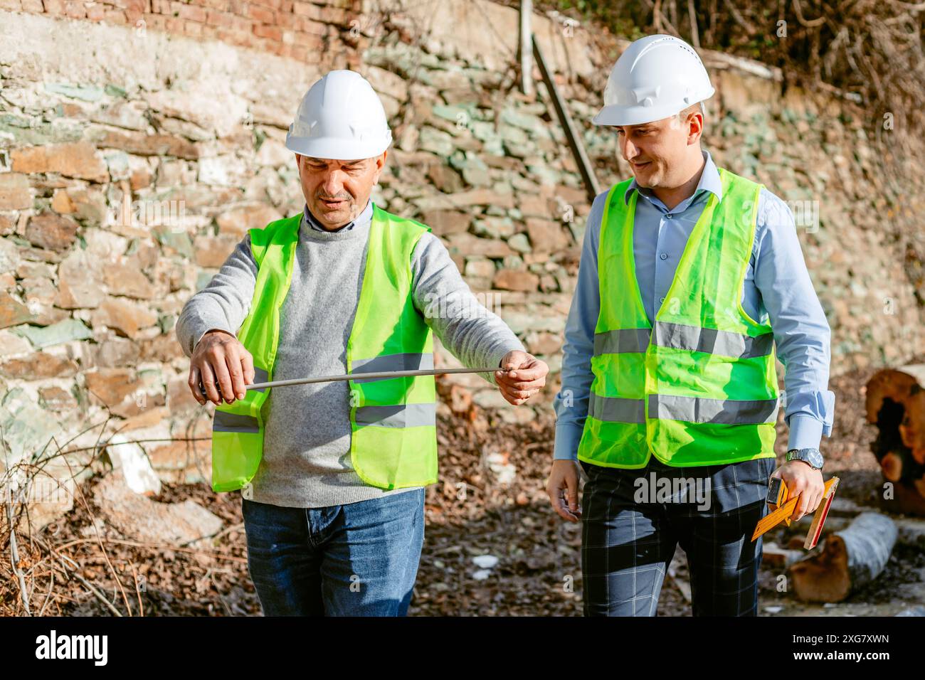Two construction workers, wearing hard hats and safety vests, stand on ...