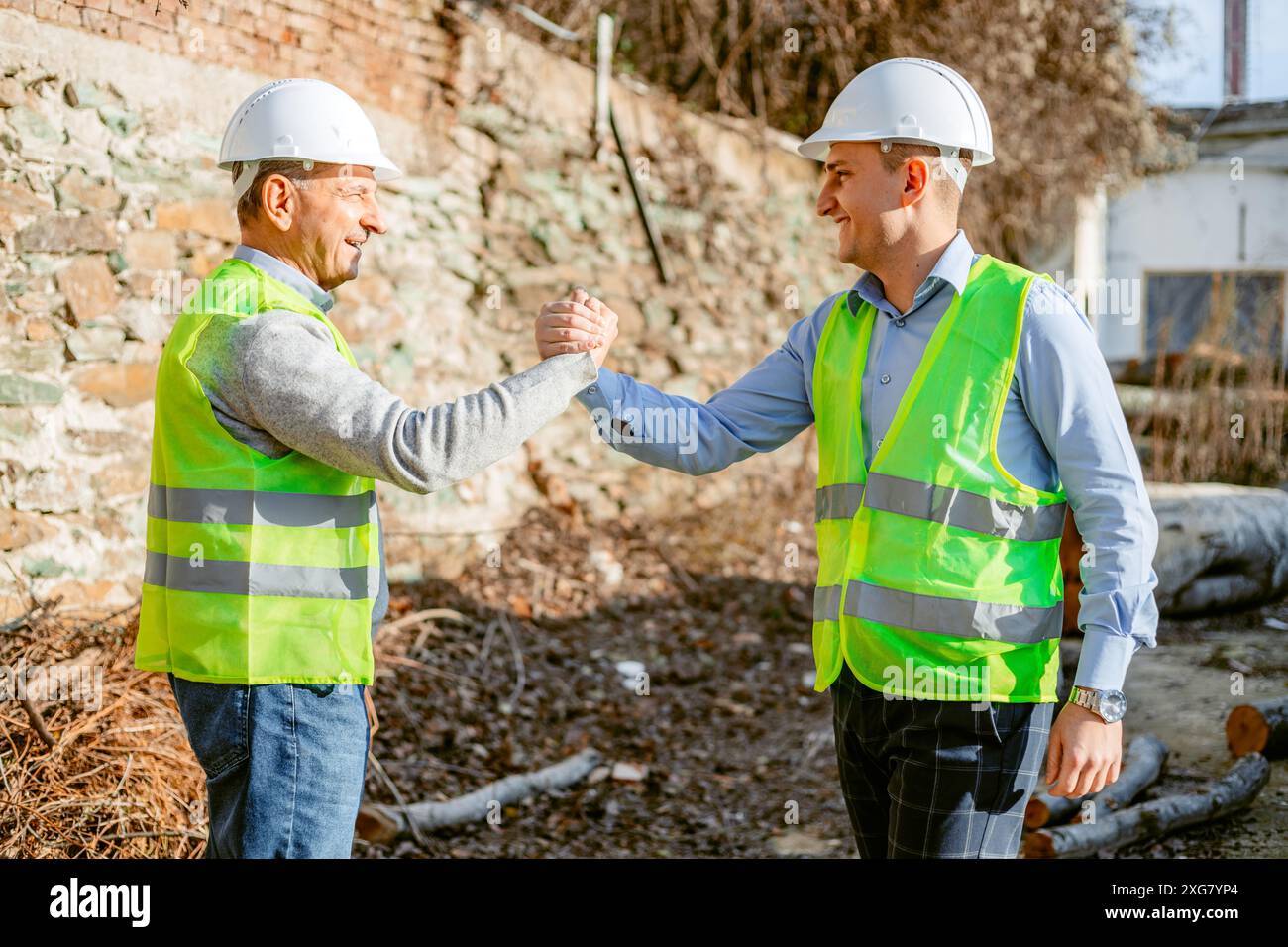 Two construction workers wearing hard hats and safety vests shake hands ...