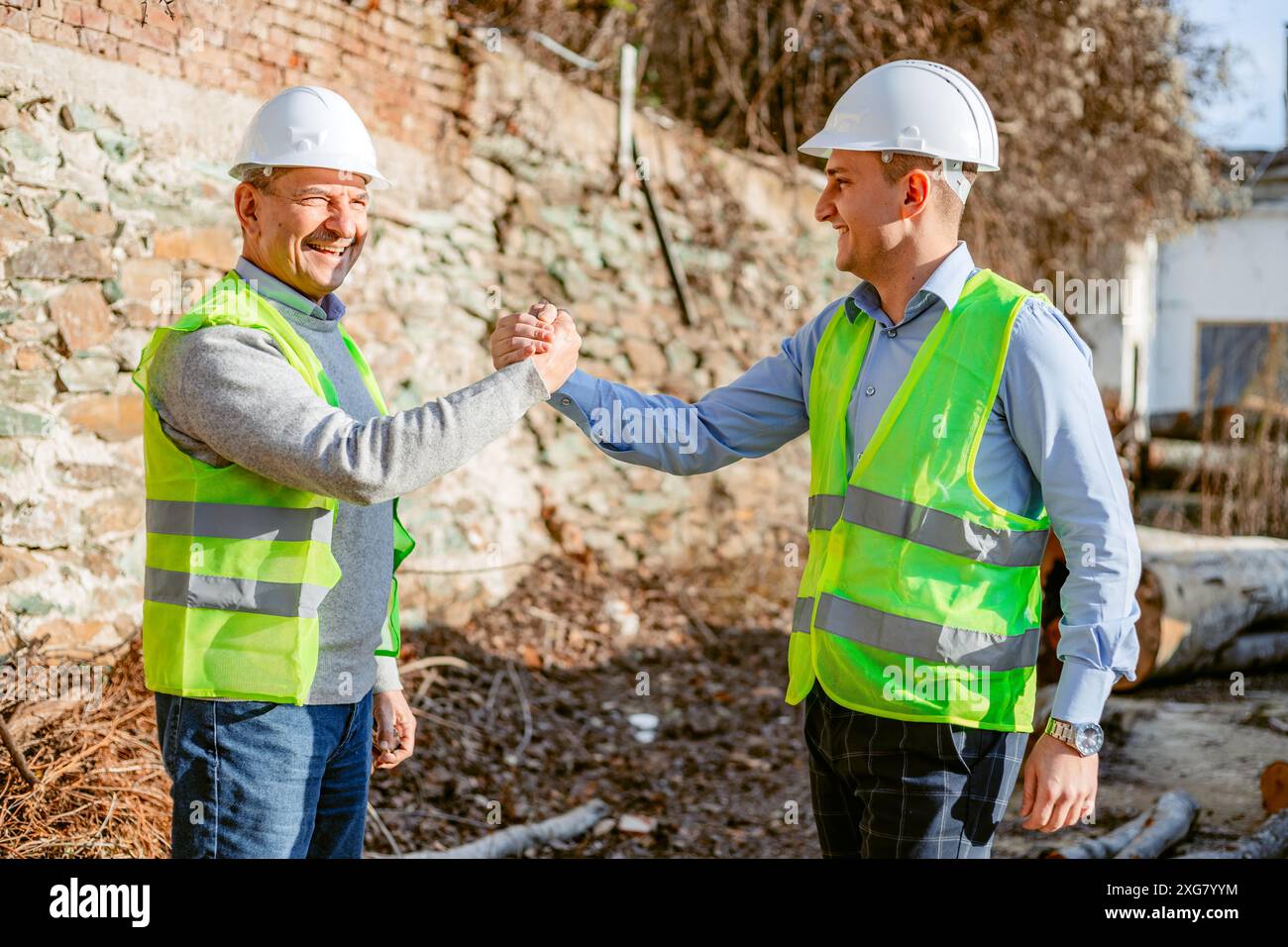 Two construction workers, wearing white hard hats and yellow safety ...
