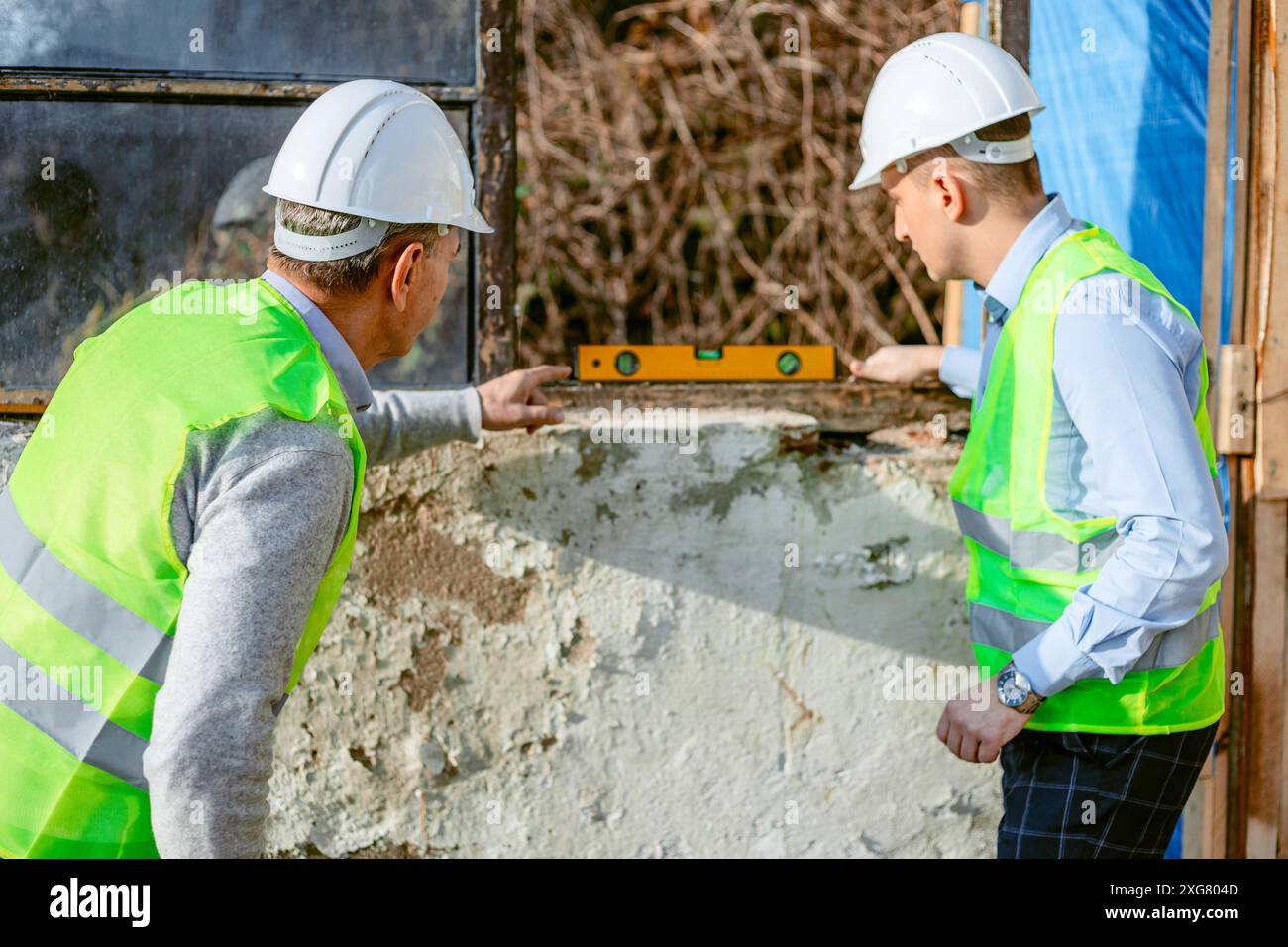Two construction workers, both wearing white hard hats and neon green ...