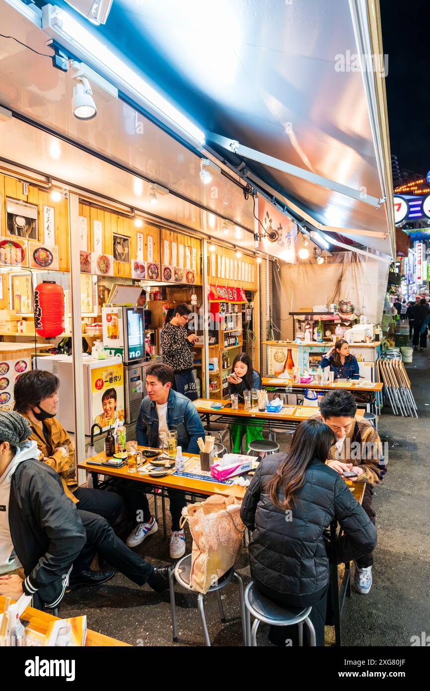 Diners sitting at tables on the pavement outside a Japanese yakitori ...