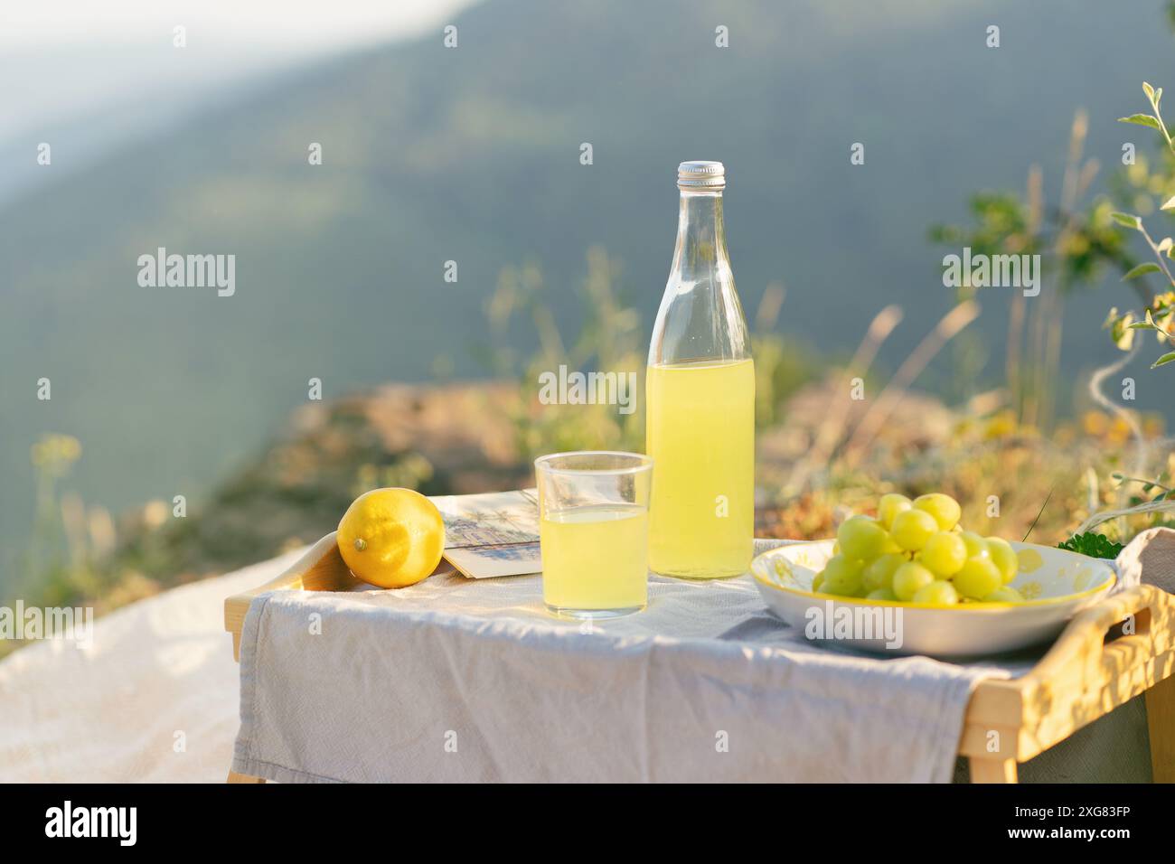 A serene summer picnic scene with lemonade, a lemon, and grapes on a ...