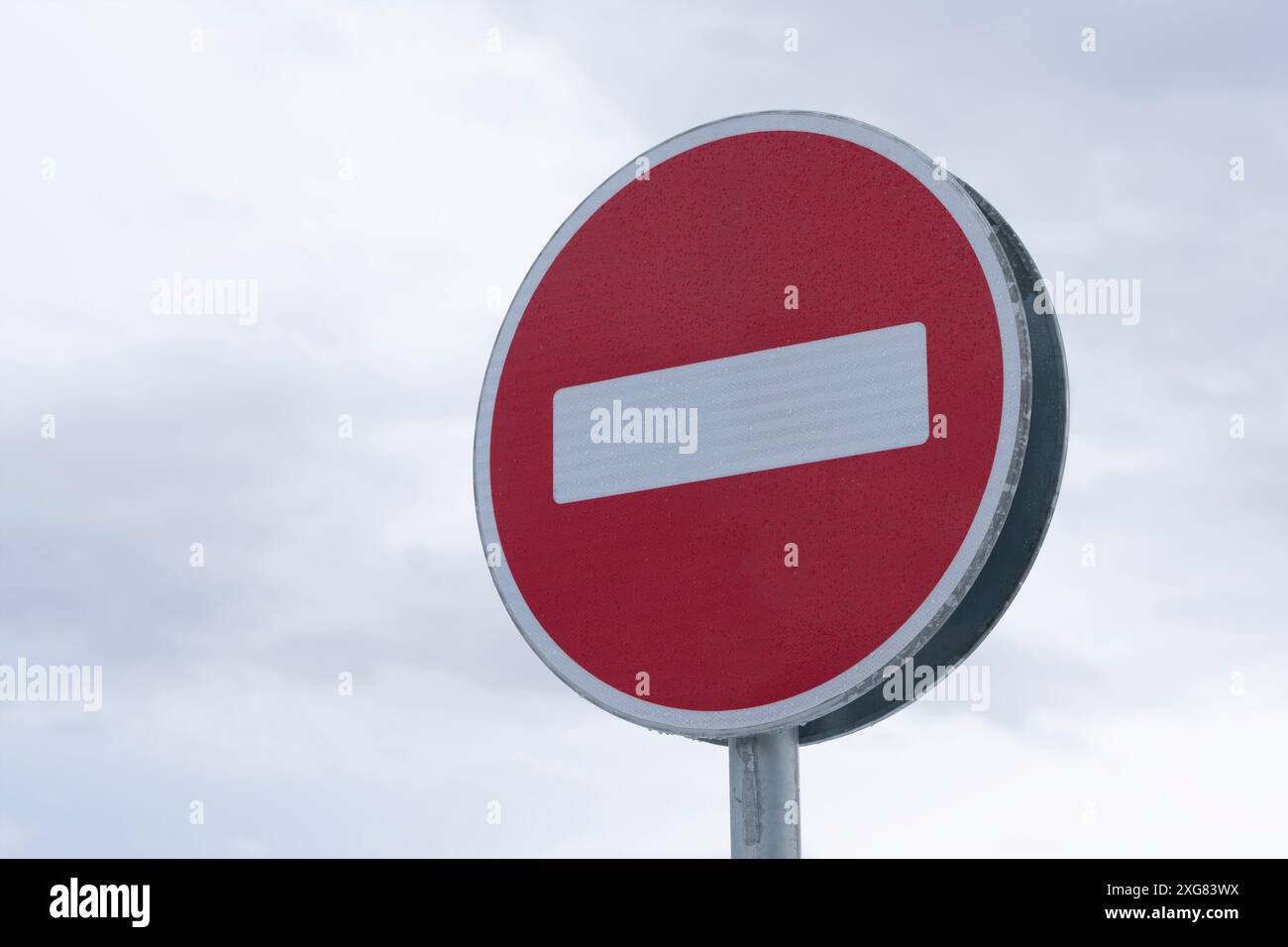 Red circular no entry road sign against a cloudy sky, depicting ...