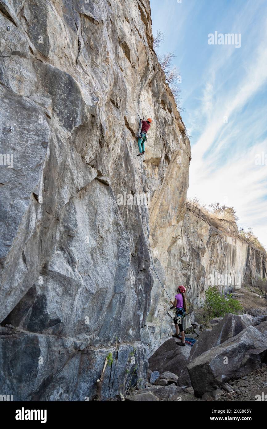 Two climbers face a steep rock face. One ascends the cliff while his ...