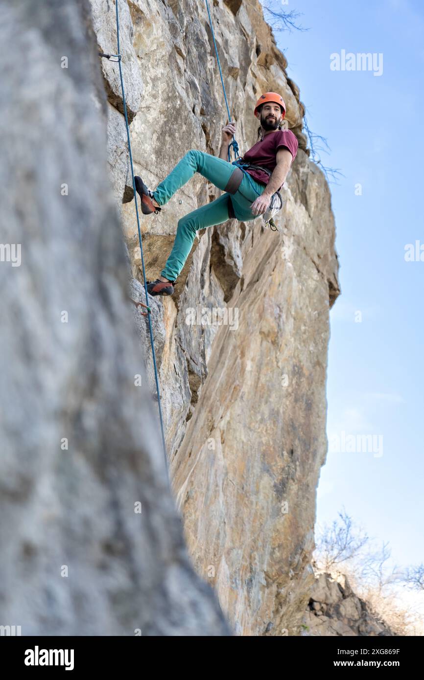 A young man climbs a challenging cliff route, secured by a rope ...