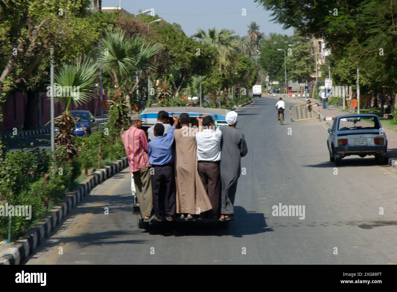 A group of men hitch a ride on the back of a vehicle in Luxor, Egypt ...