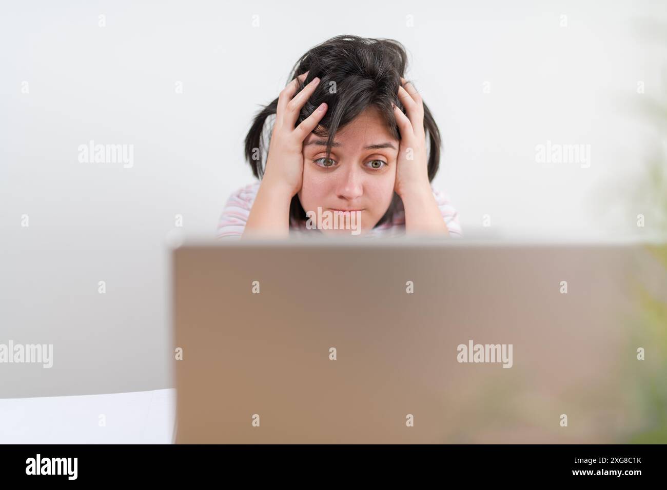A young student frustrated in front of the computer with hand on head ...