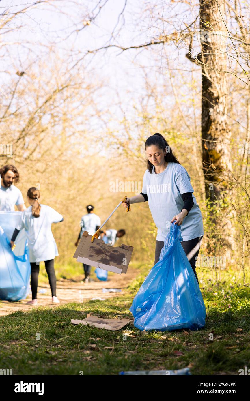 Woman environmentalist grabbing rubbish with a claw tool in the woods ...
