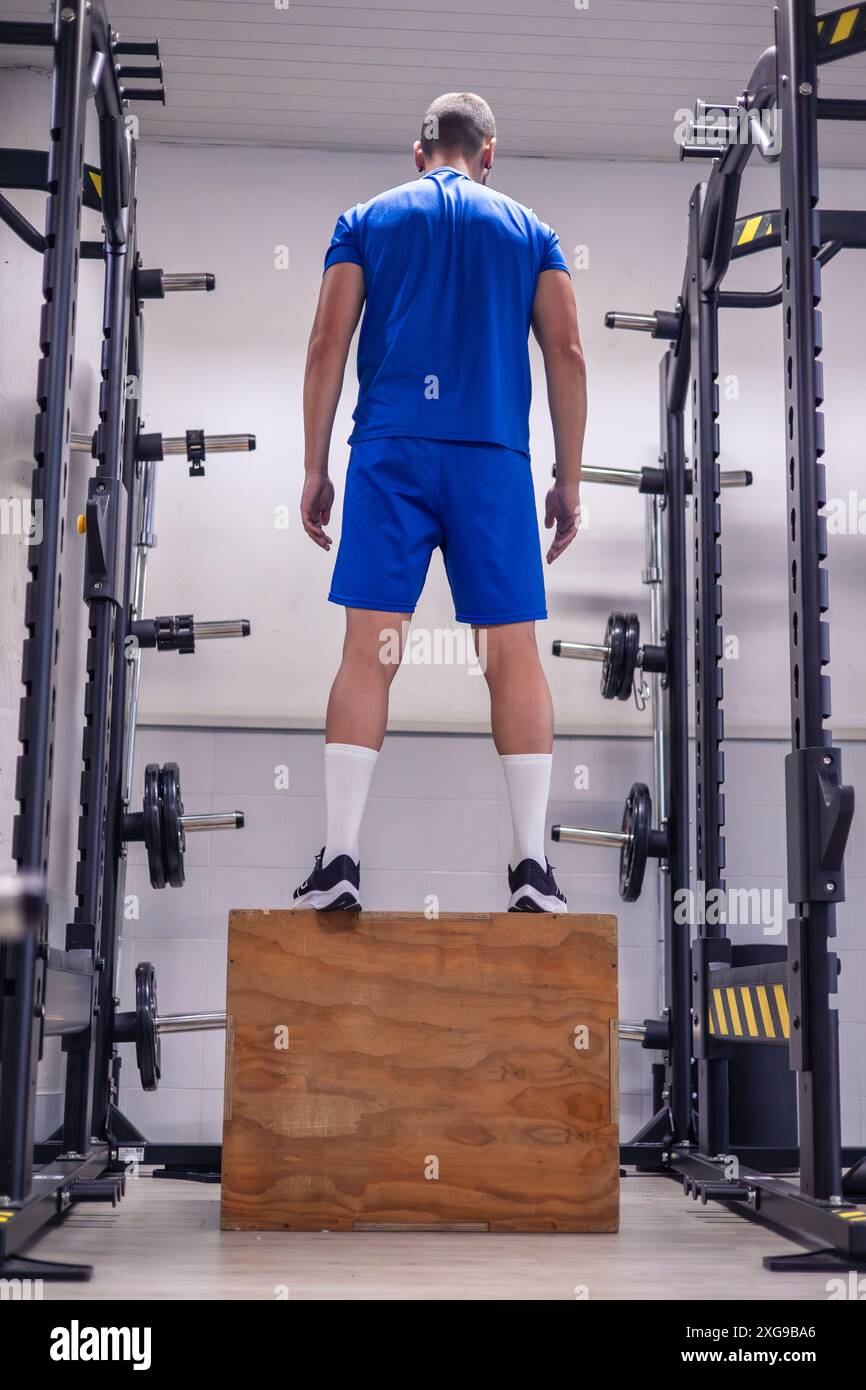young fitness athlete is seen from behind, standing on a plyometric ...