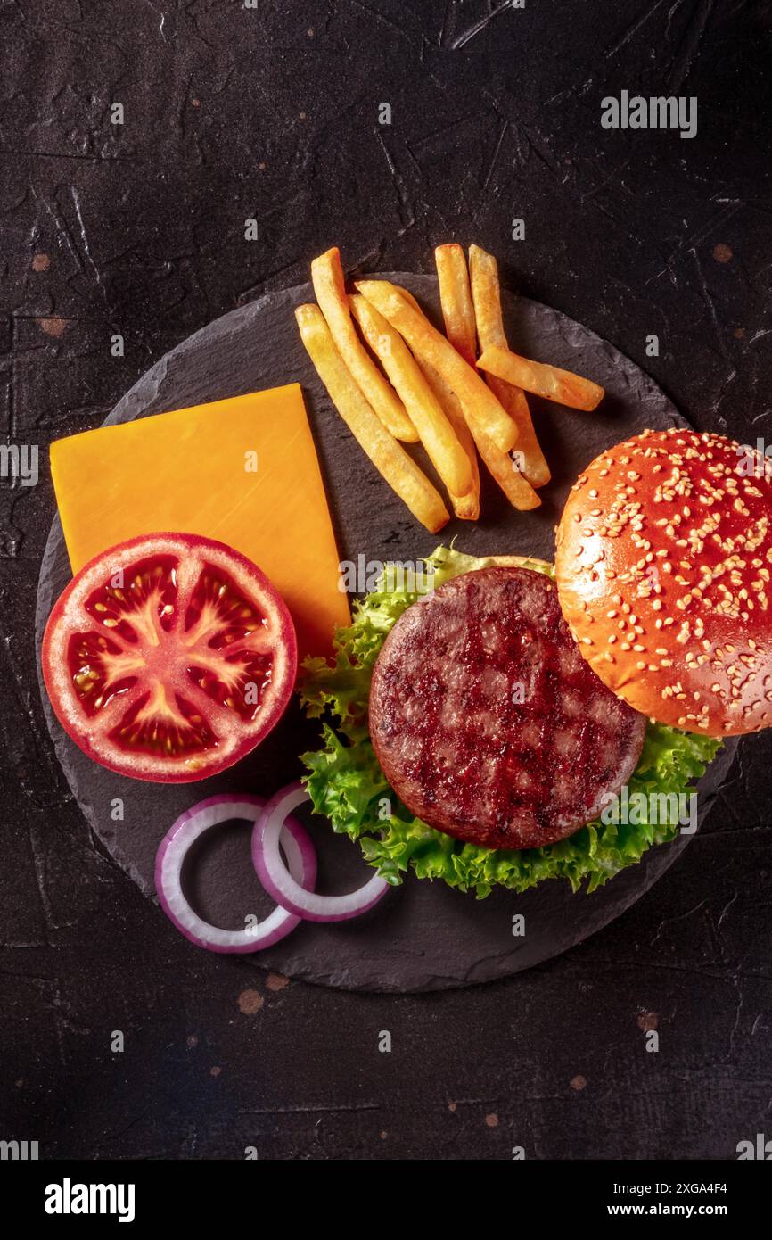 Beef burger ingredients, shot from above on a dark background ...
