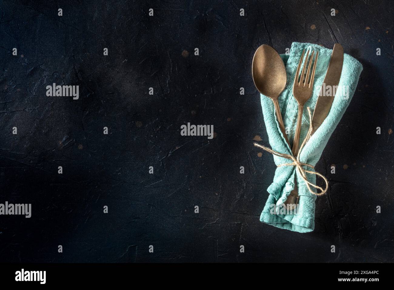 Cutlery. A spoon, a fork, and a knife in a teal napkin on a black slate ...