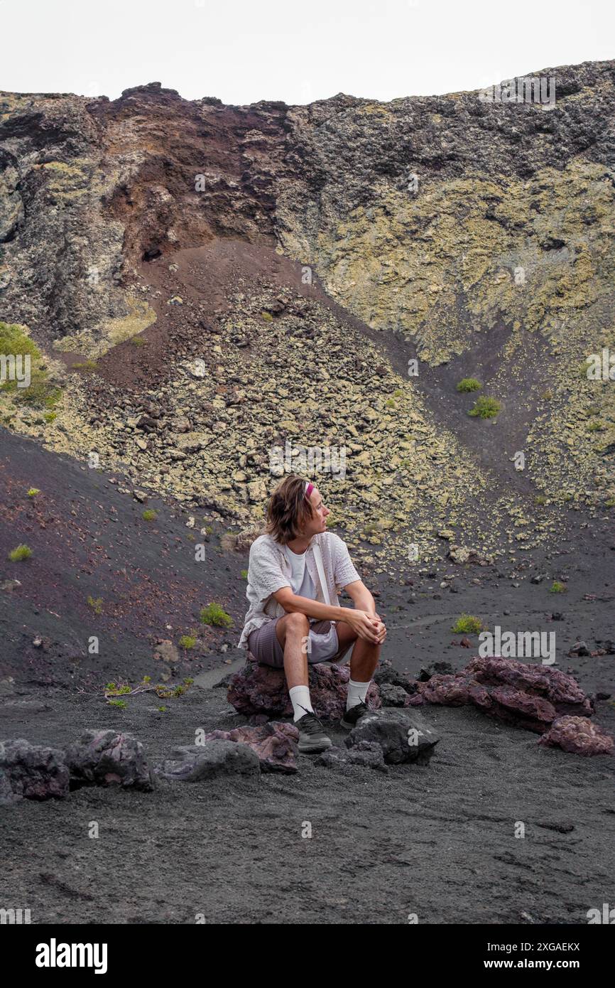 A young man sits on volcanic rock at the base of El Cuervo volcano in ...
