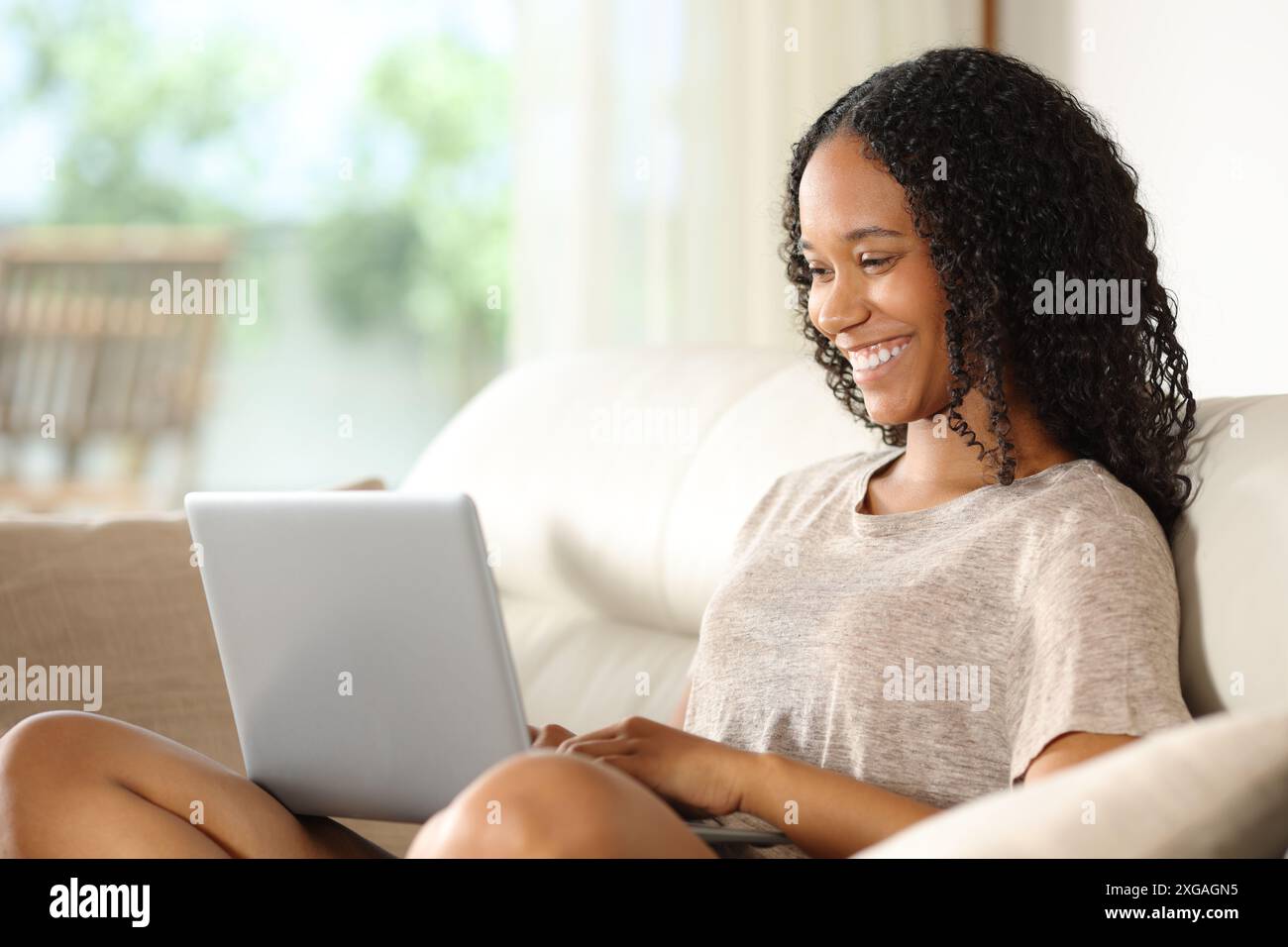 Happy black woman using laptop sitting on a couch at home Stock Photo ...