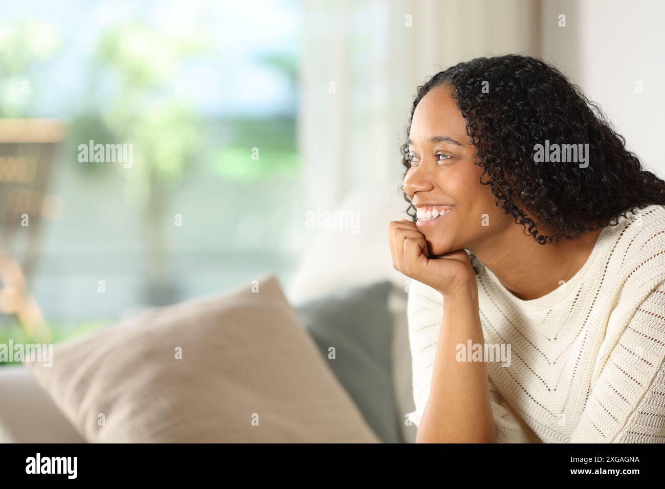 Happy black woman contemplating the garden through a window in a luxury ...