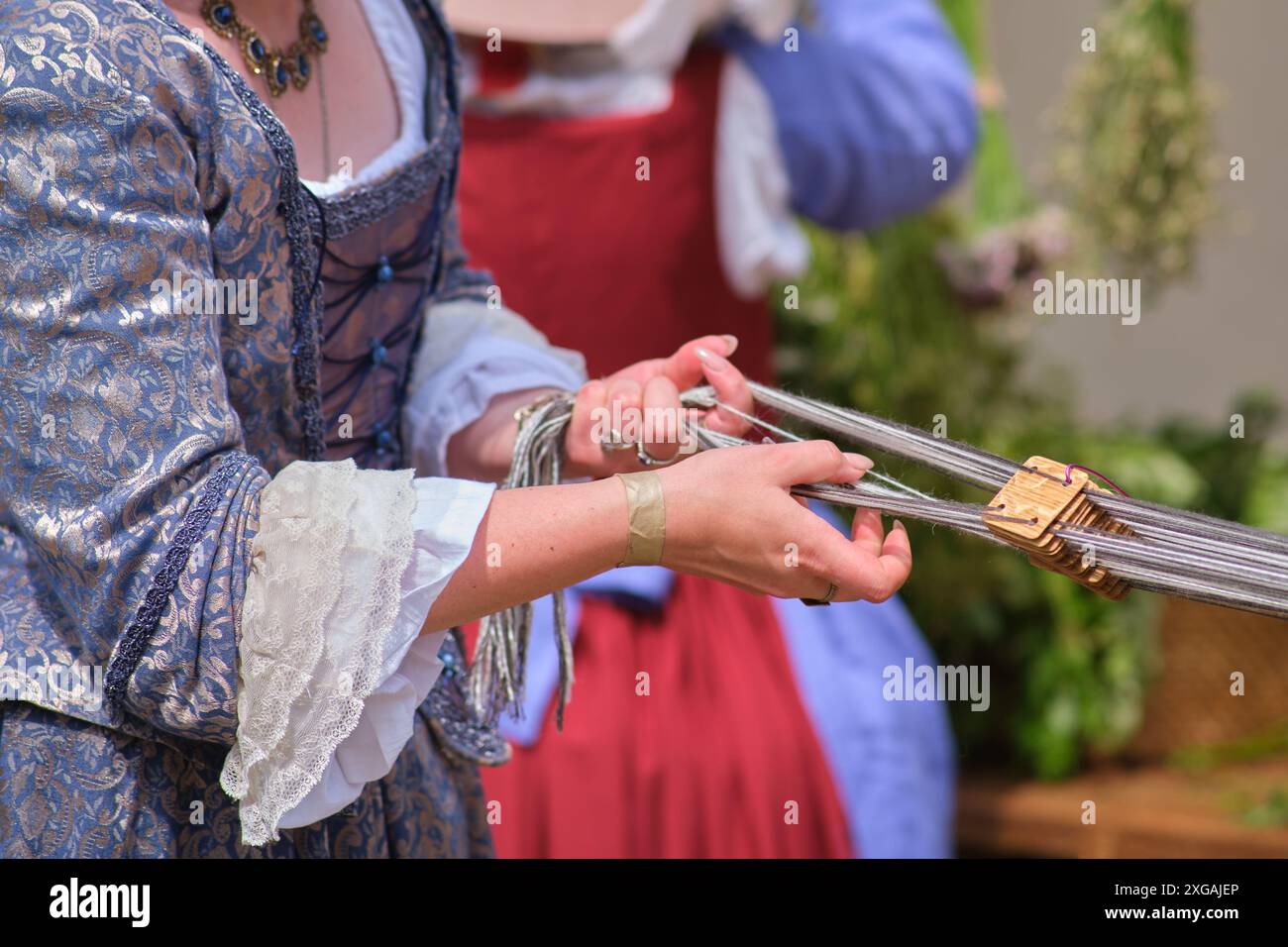 A person in historical attire is weaving using a wooden tablet weaving ...