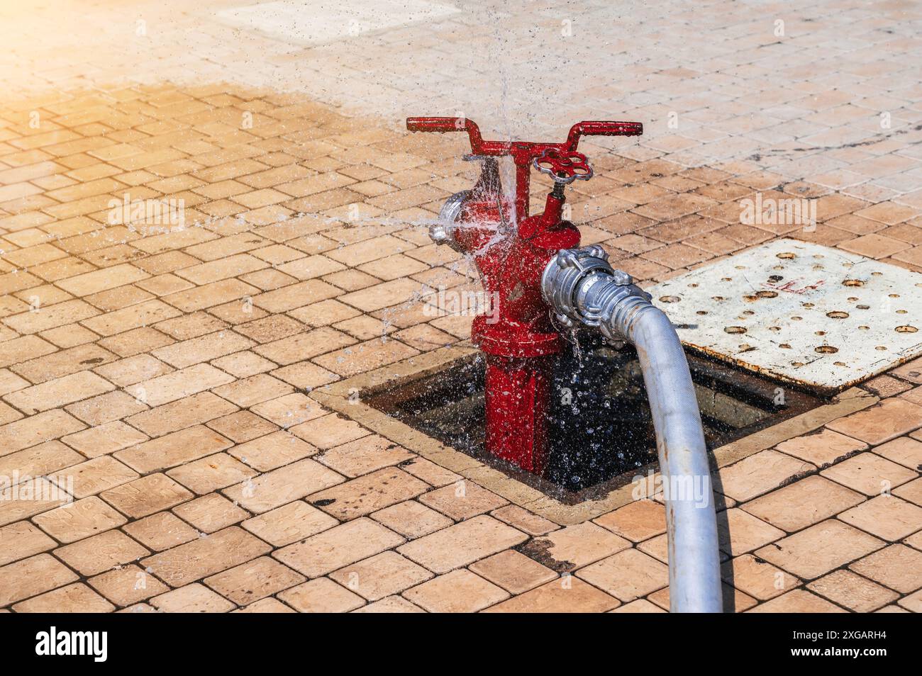 red fire hydrant with connected hose with splashing water for ...