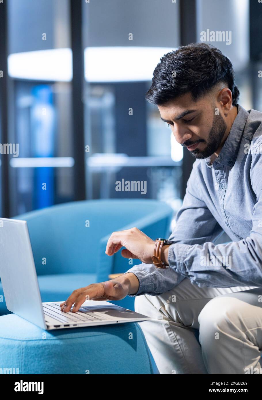 Using laptop, man checking time on smartwatch while working in modern ...