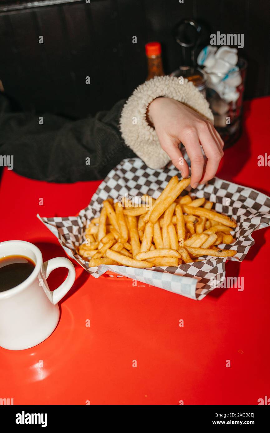 Hand picking fries from checkered basket on red diner table Stock Photo ...