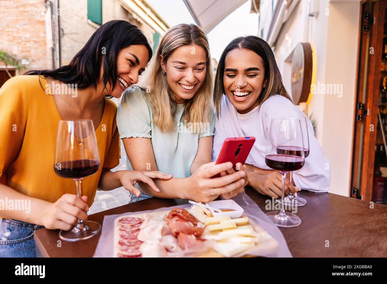 Three young women using mobile phone while enjoying appetizer in a bar ...