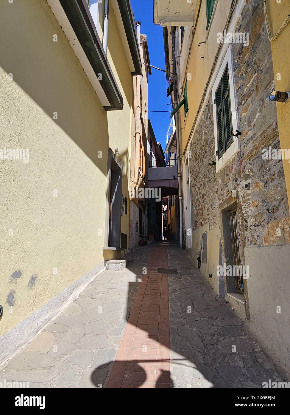 Vertical image of narrow alley in Manarola, Italy. Blue sky visible ...