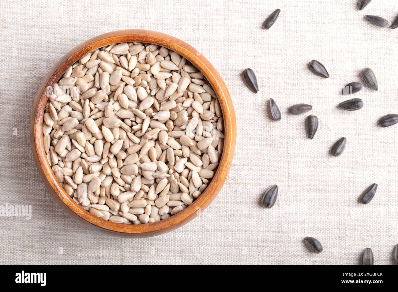 Hulled sunflower seeds in a wooden bowl on linen fabric. Fruits of the ...