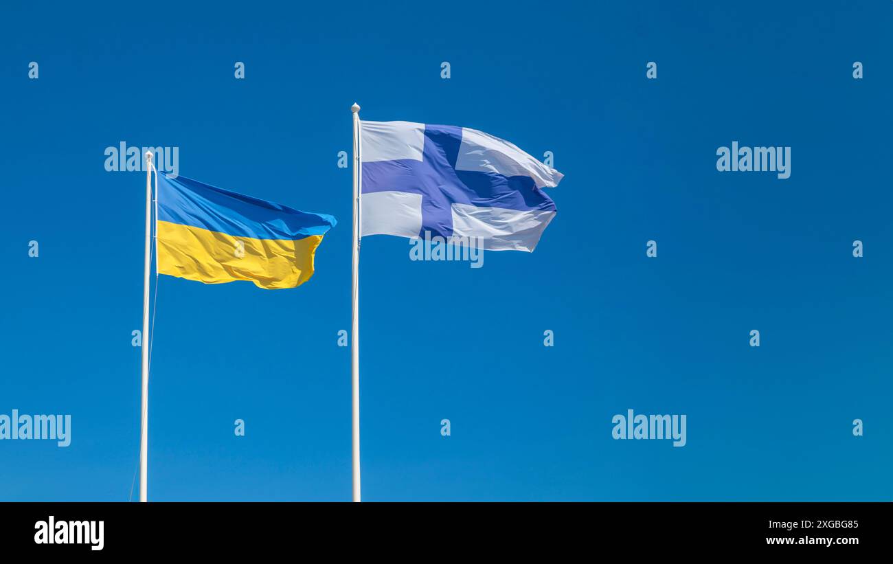 Ukraine and Finland waving in wind and sunlight flags on the clear blue ...