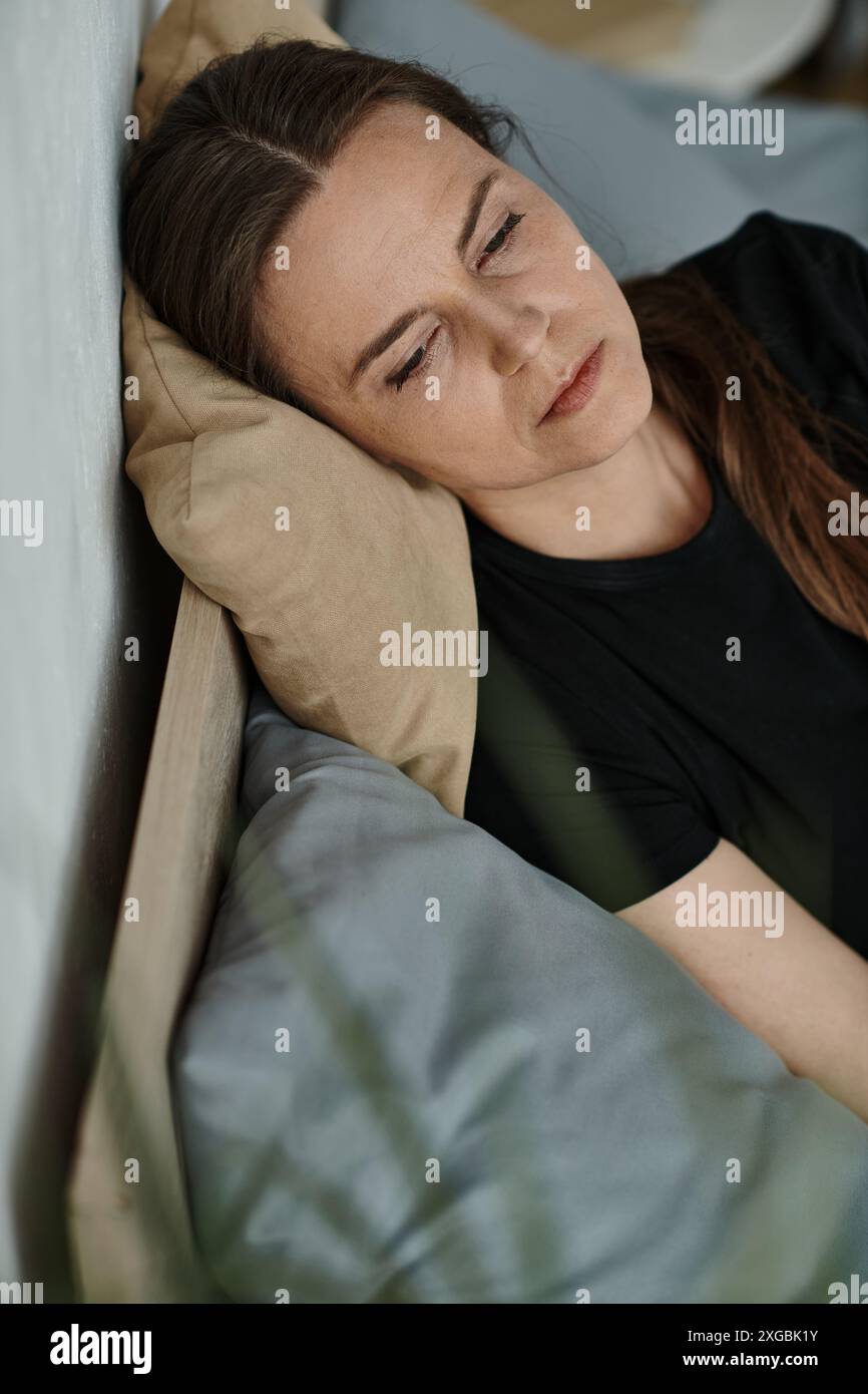 A middle-aged woman finds solace in bed, her eyes gently closed in ...