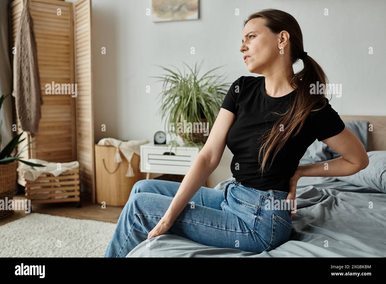 Woman sitting on bed, clutching her lower back in pain, struggling with ...