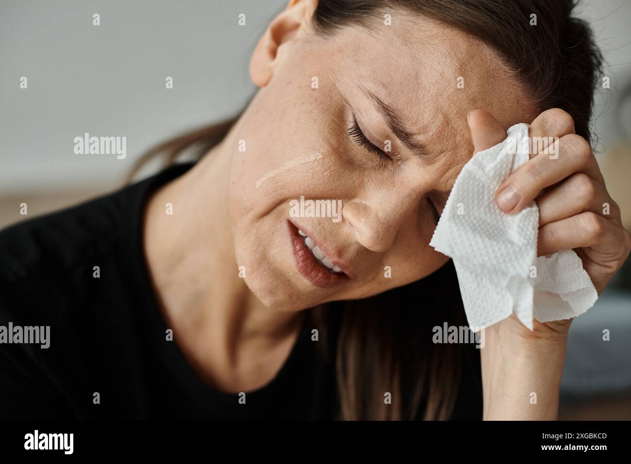 A middle-aged woman wiping her face with a tissue in a moment of ...