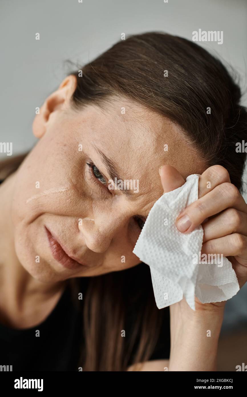 Middle aged woman wiping her face with a tissue during a moment of ...