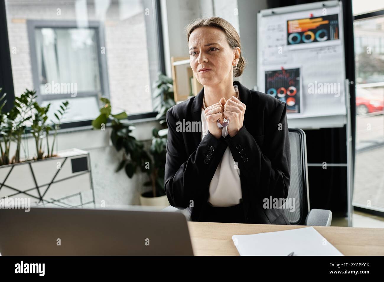A middle-aged woman sits at a desk, staring at her laptop screen in ...